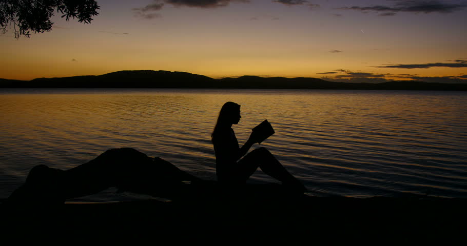 Silhouette Of A Young Woman Siting Near The Lake And Reading A Book At ...