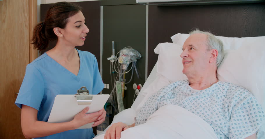 Nurse Sitting At Bedside Of Senior Male Patient Discussing Case Using ...