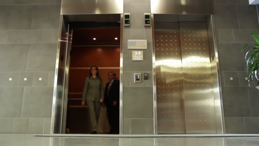 Business People Get Out Of An Elevator And Walk Through Building Atrium ...